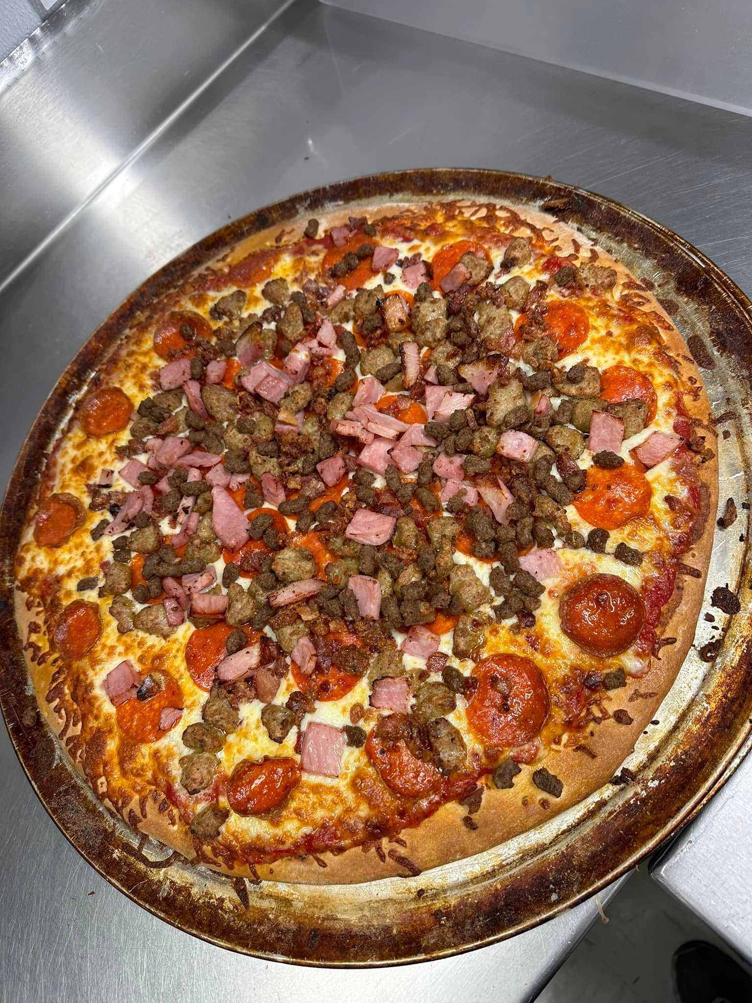 A freshly baked pizza topped with pepperoni, diced ham, and sausage on ...